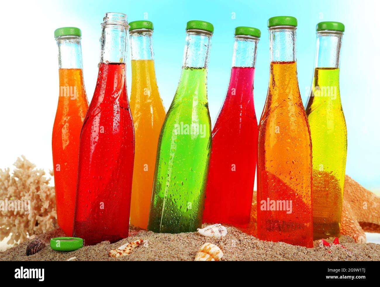 Bottles of tasty drink on sand on bright background Stock Photo - Alamy