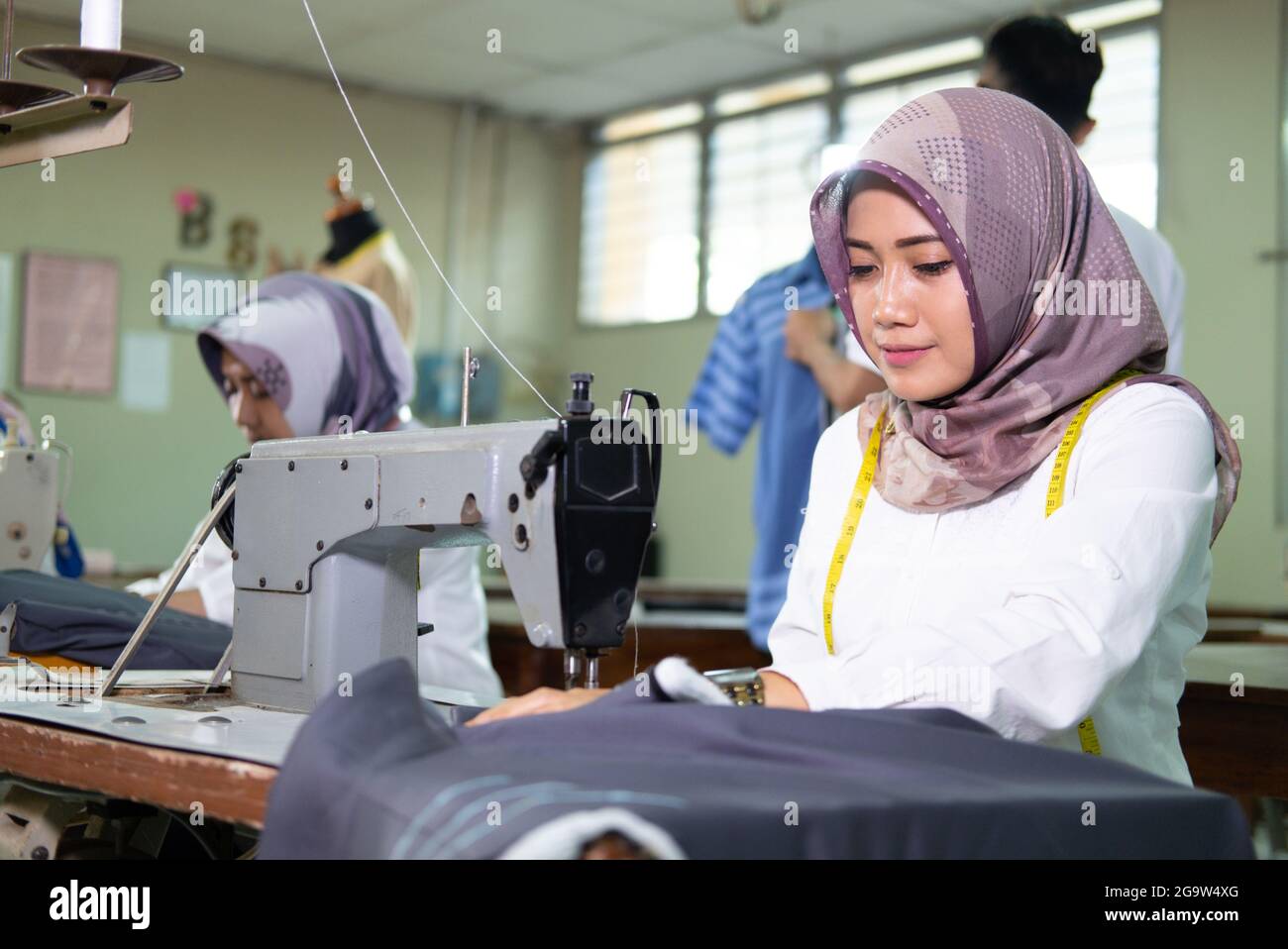 close up female tailor in hijab using a sewing machine while workin ...