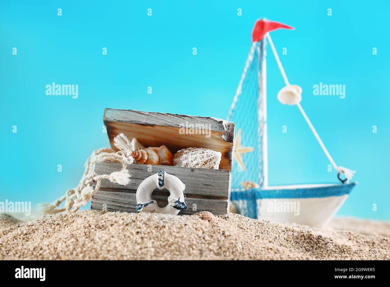Marine still life with toy model of ship on sand on blue background ...