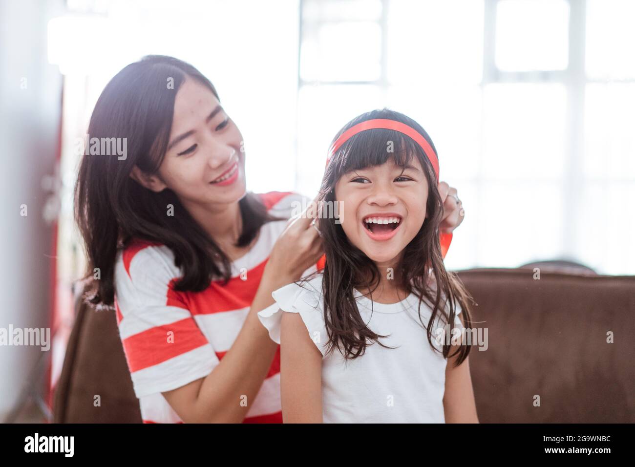 mom tying red ribbon on her daughter's forehead Stock Photo - Alamy
