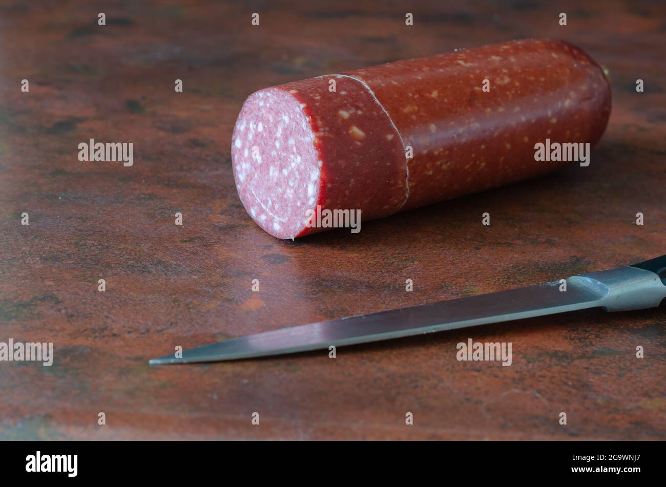Salami and a kitchen knife on a red countertop. Half of a sausage stick ...