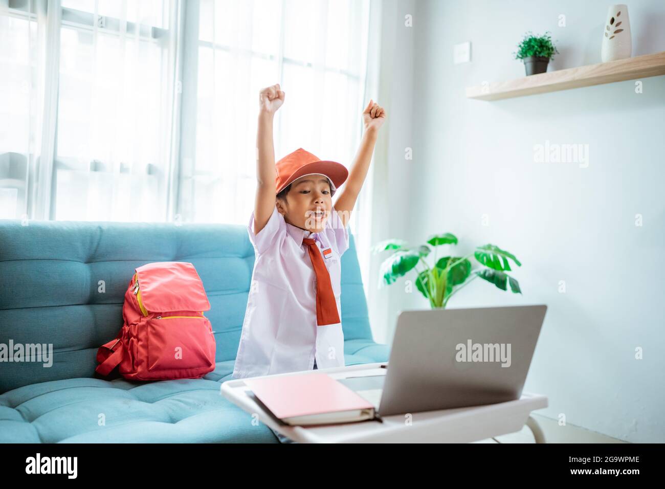 excited primary school student with uniform raise her arm during online ...