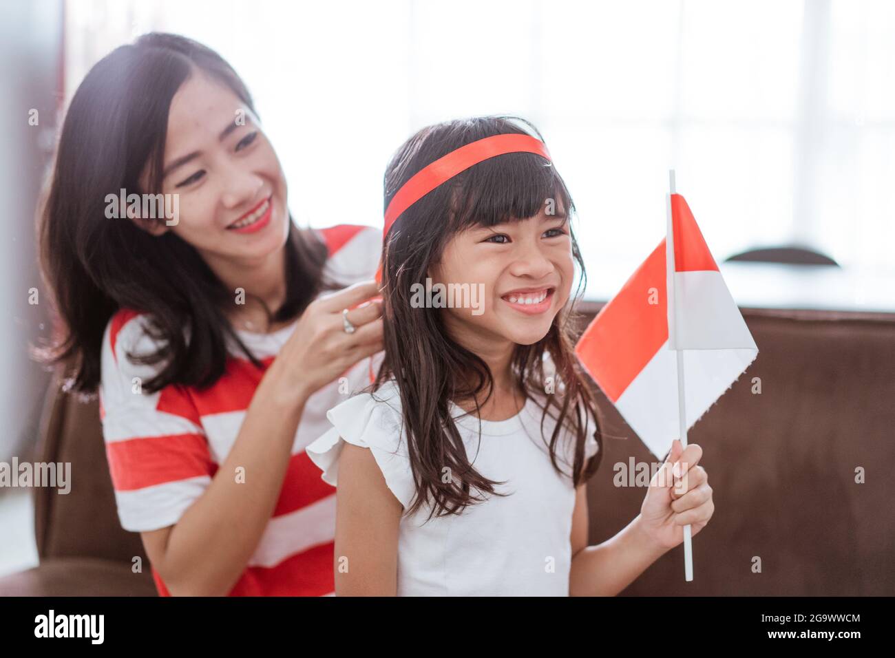 mom tying red ribbon on her daughter's forehead Stock Photo - Alamy