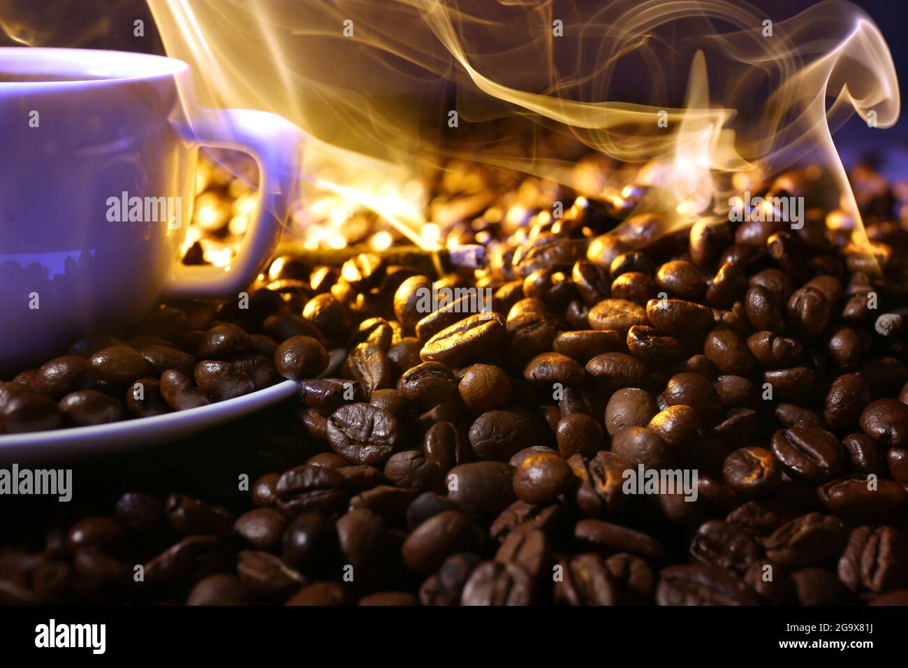 Pile of coffee beans and cup of hot coffee in beam on dark background ...