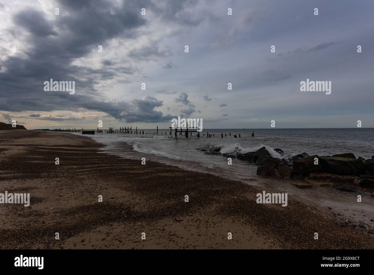 cloudy gray sky over the beach with rocks and wooden anchorage posts on ...