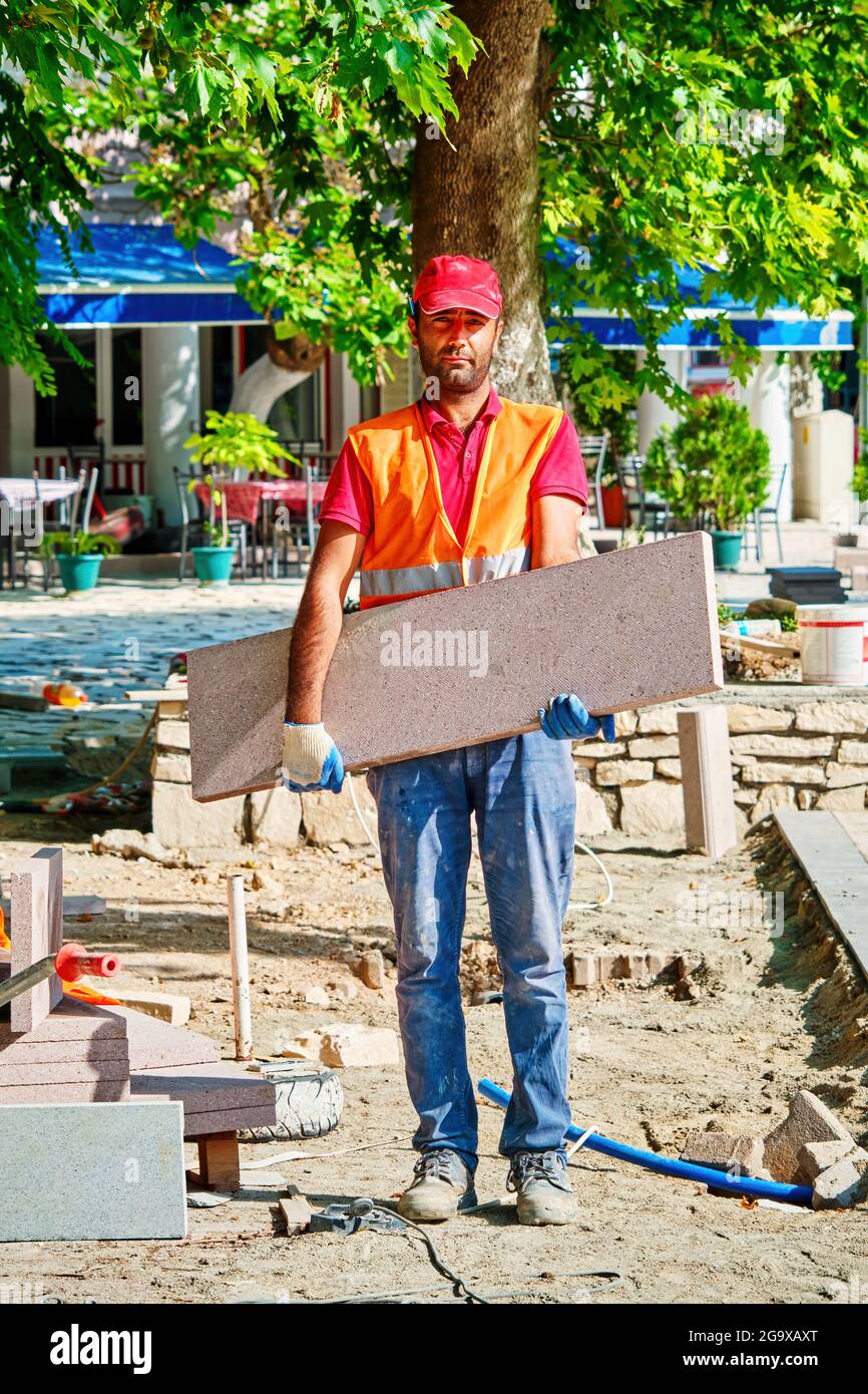 Turkish pavement construction worker holds a big tile of pavement stone ...