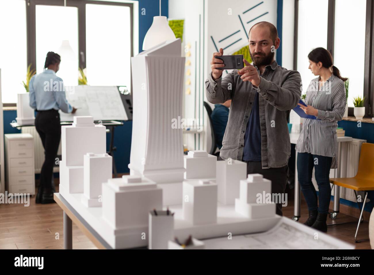 Architect Profession Man Looking At Maquette Layout Using Smartphone To Design Building Model
