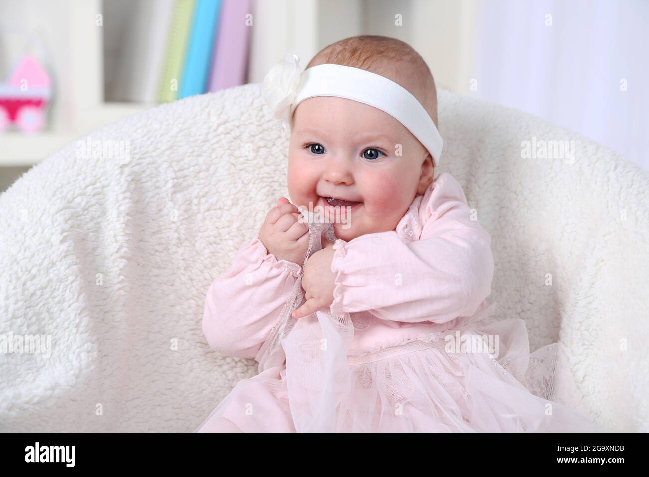 Cute baby girl in pink dress sitting in arm-chair, on home interior ...