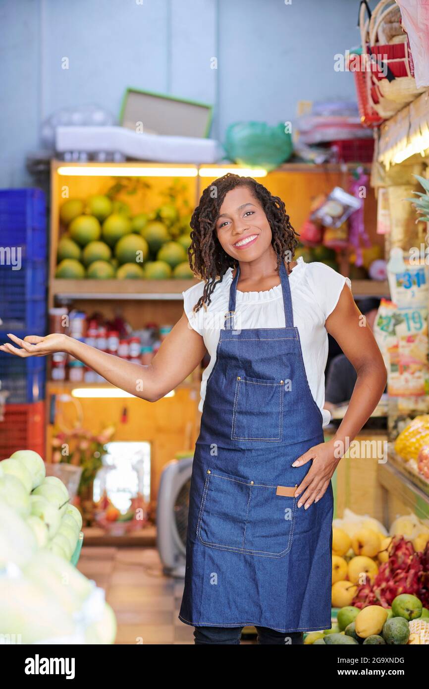 Portrait of African saleswoman in apron smiling at camera while working ...
