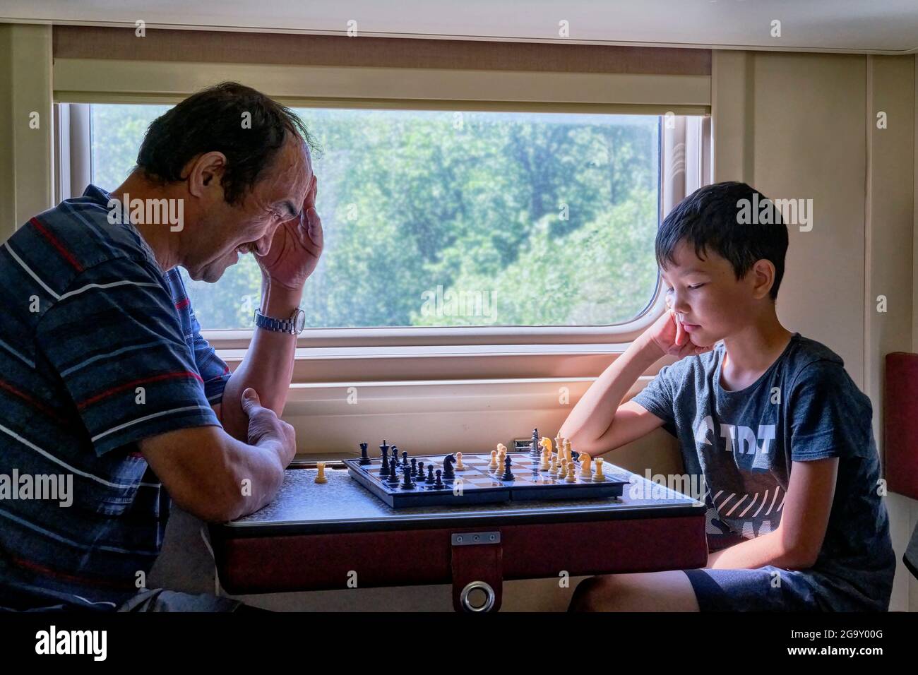 Asian young boy and senior man playing chess at train Stock Photo - Alamy