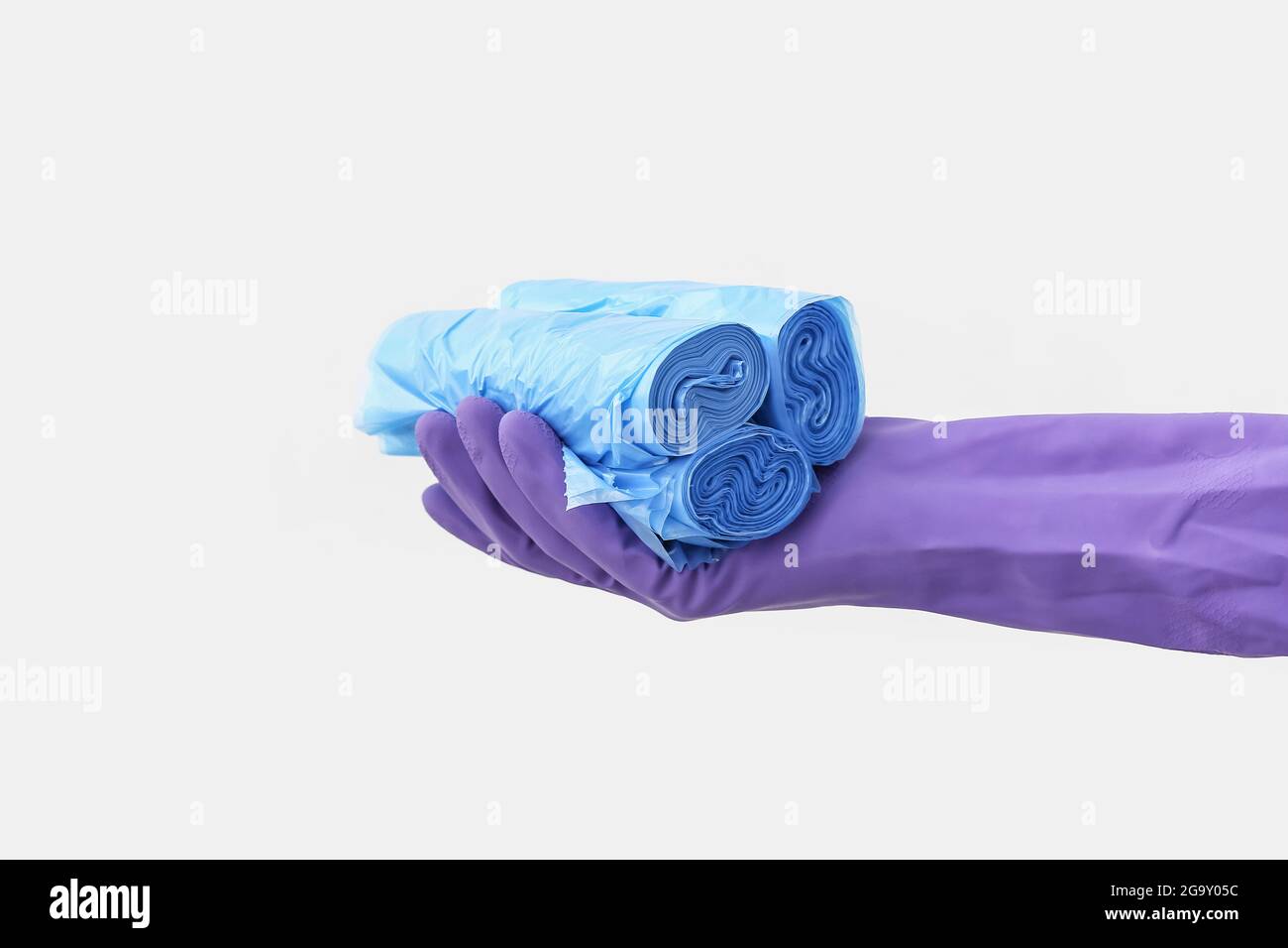 Hand in rubber glove with rolls of garbage bags on white background ...