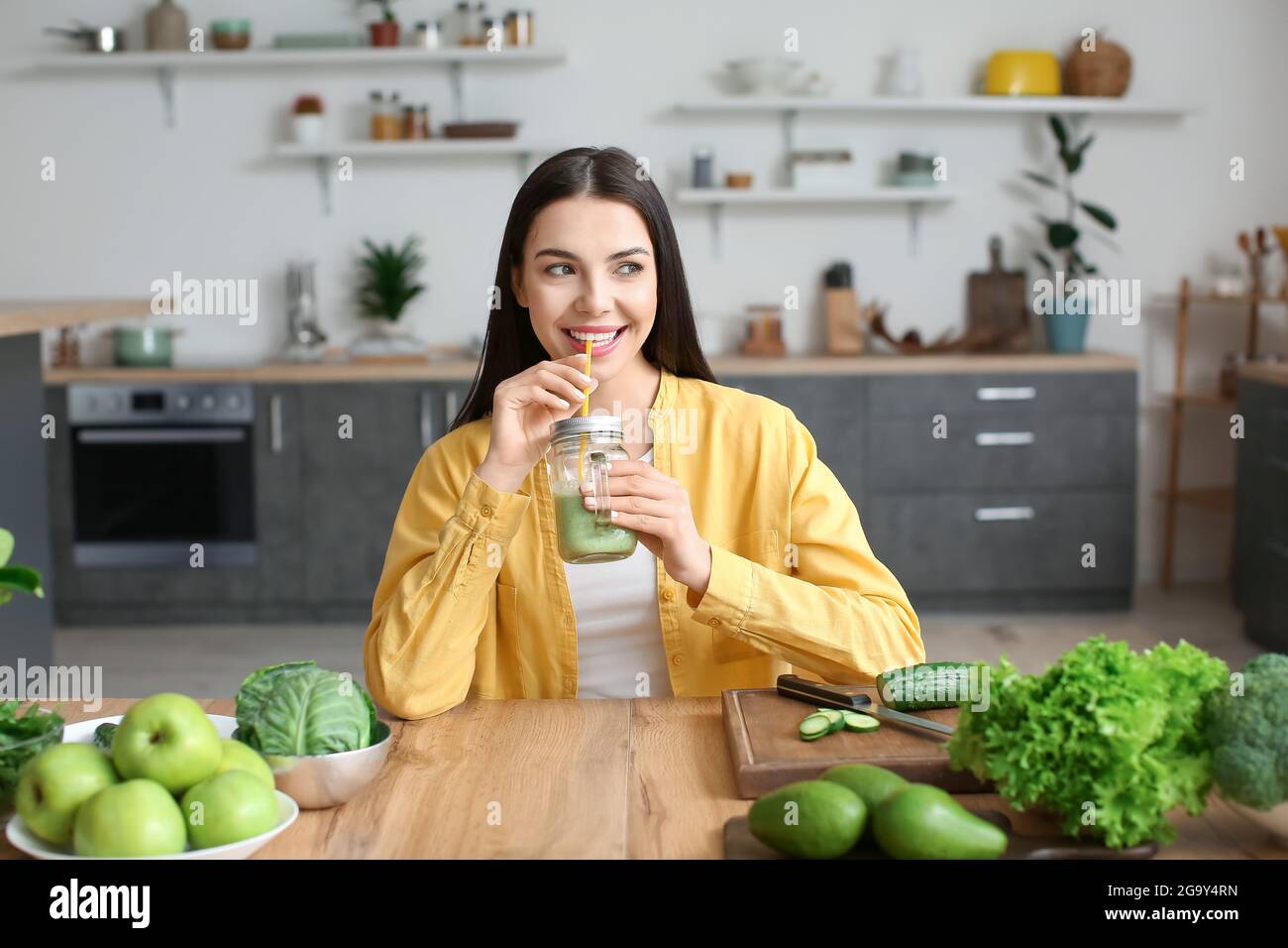 Young woman drinking healthy green smoothie in kitchen Stock Photo - Alamy