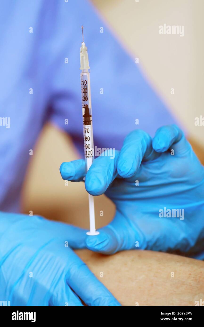 The nurse makes an injection with the vaccine to the patient at home ...
