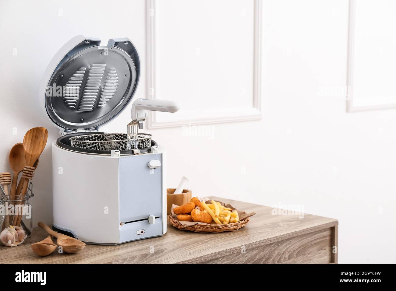 Modern deep fryer, french fries, nuggets and kitchen utensils on table ...