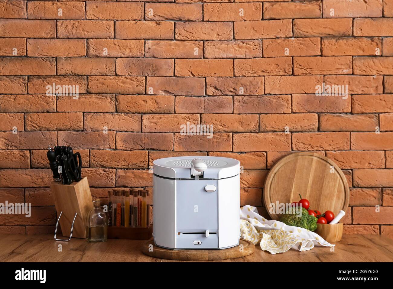 Modern deep fryer, kitchen utensils and products on table near brick ...