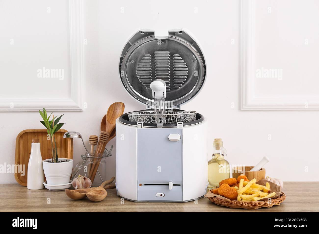 Modern deep fryer, french fries, nuggets and kitchen utensils on table ...