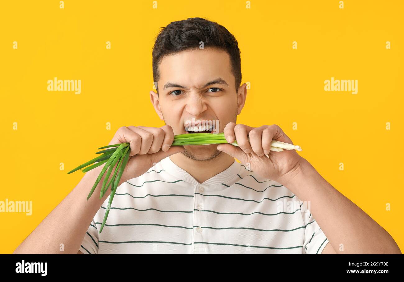 Emotional young man eating green onion on color background Stock Photo ...