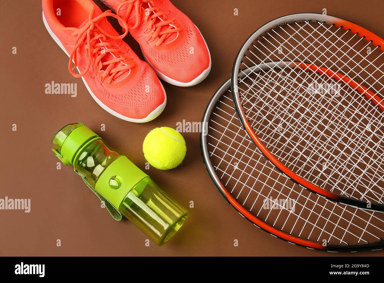 Sport shoes, bottle of water, tennis rackets and ball on color ...