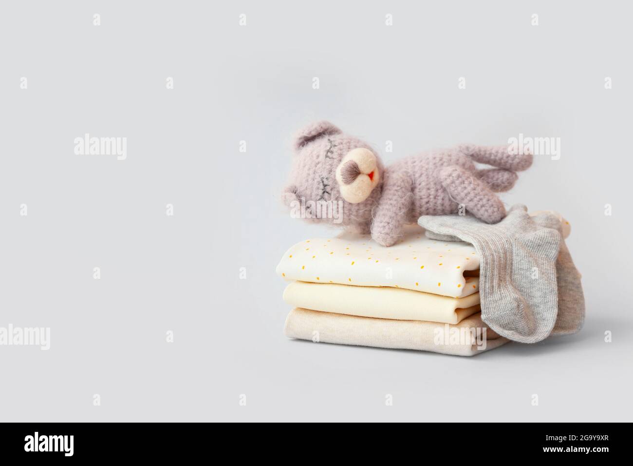 Stack of baby clothes and knitted toy on grey background Stock Photo ...