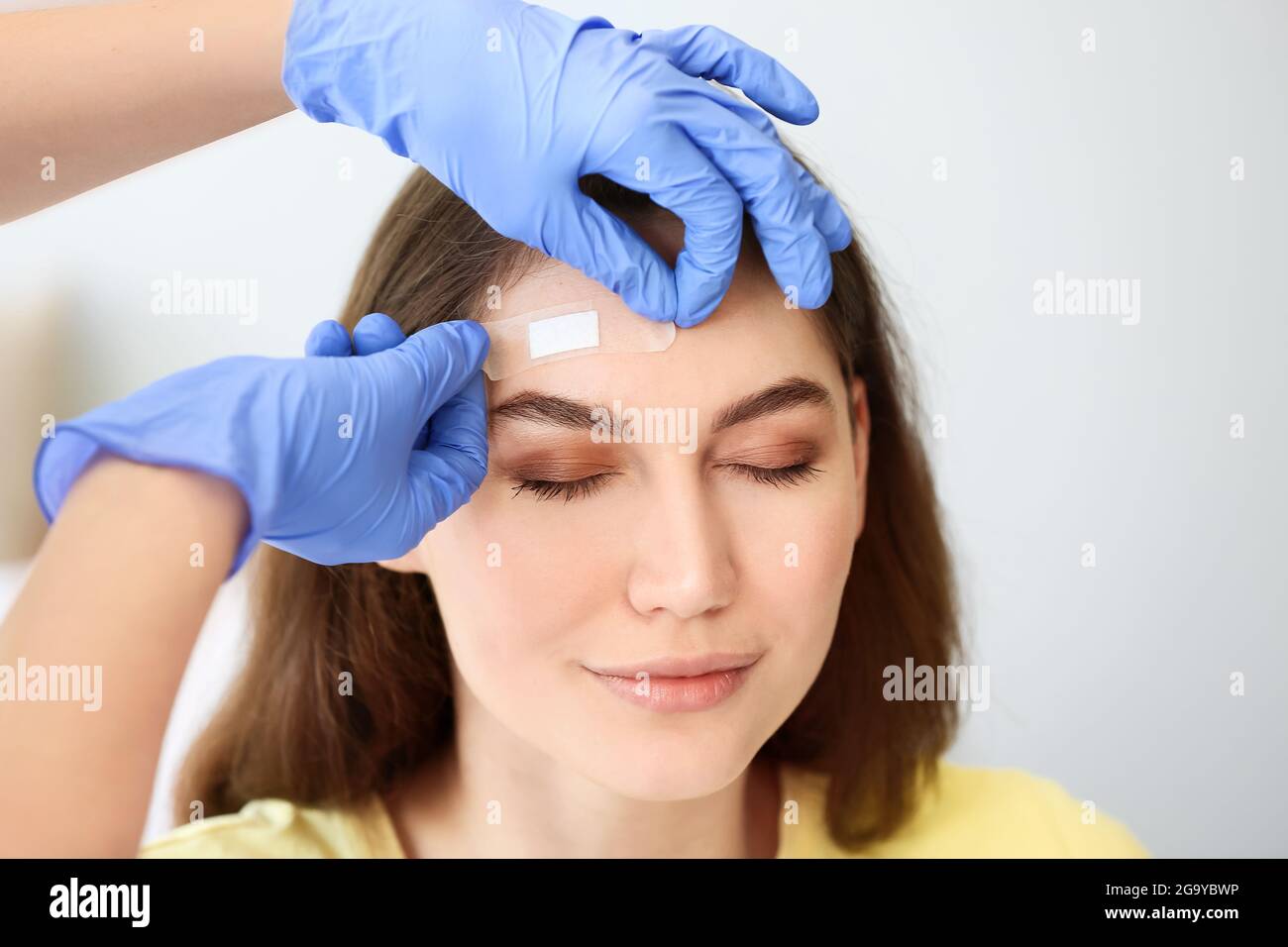 Nurse applying medical patch on young woman's forehead in clinic Stock ...
