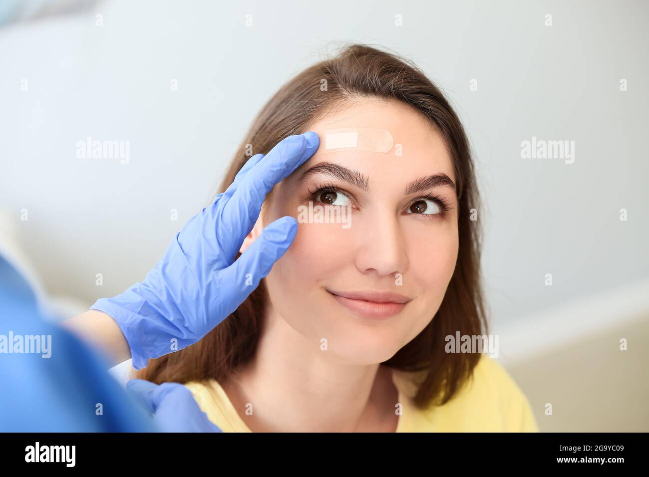 Nurse applying medical patch on young woman's forehead in clinic Stock ...