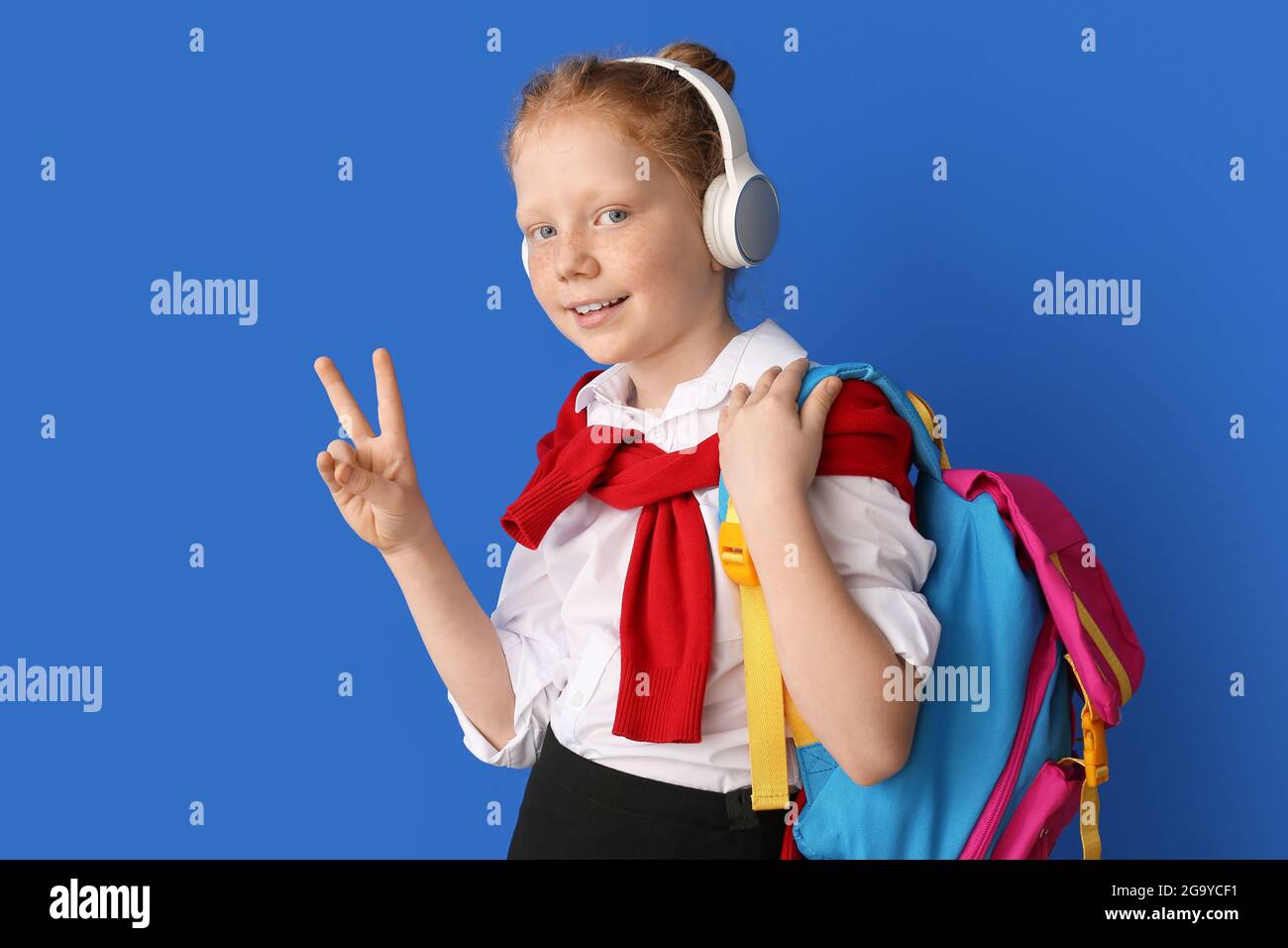 Cute little schoolgirl showing victory gesture on color background ...
