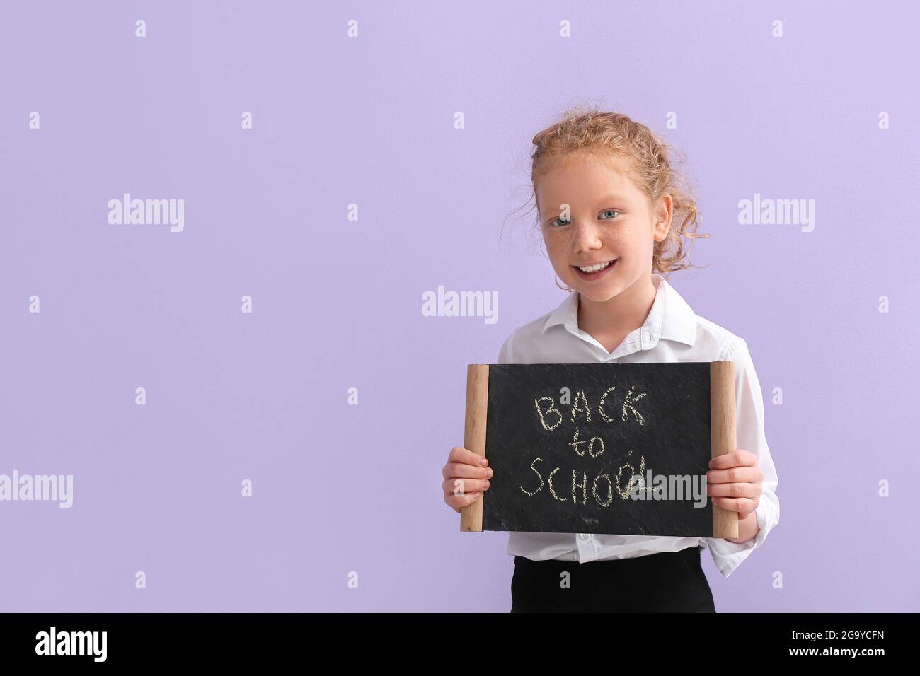 Cute little girl holding chalkboard with text BACK TO SCHOOL on color ...