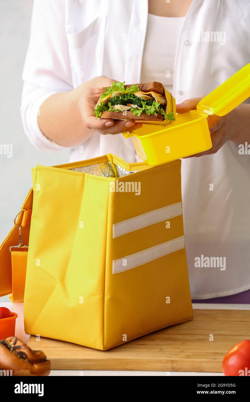 Woman packing meal into lunch box bag on light background Stock Photo ...