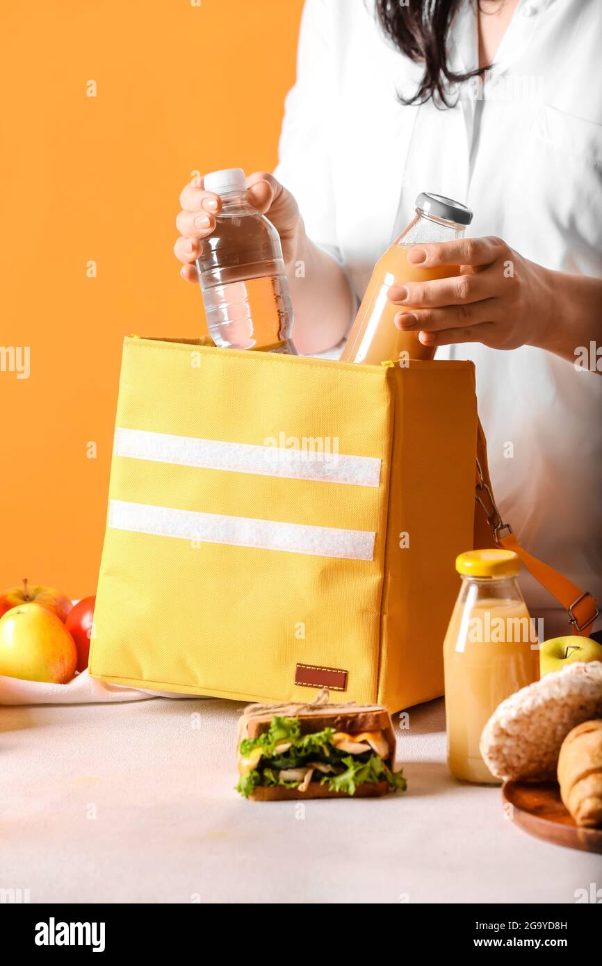 Woman packing meal into lunch box bag on color background Stock Photo ...