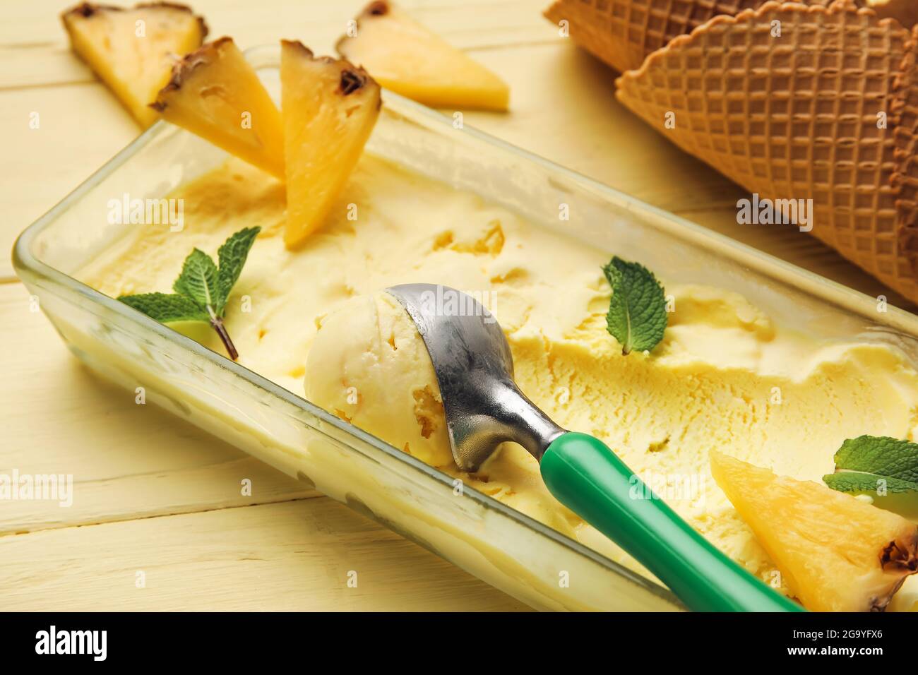 Container with tasty pineapple ice cream on color wooden background ...