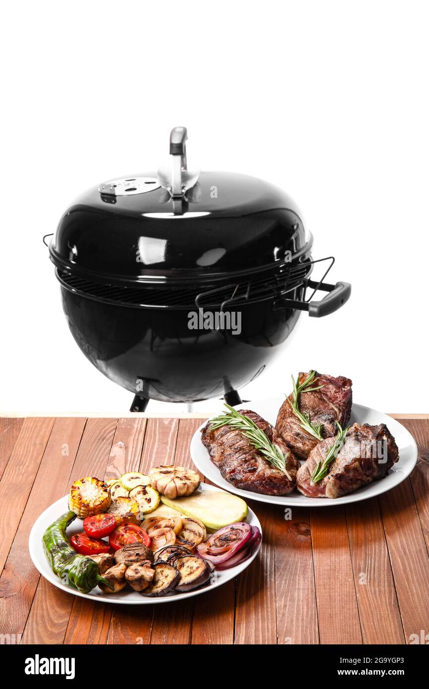 Barbecue grill and plates with tasty vegetables and steaks on table ...