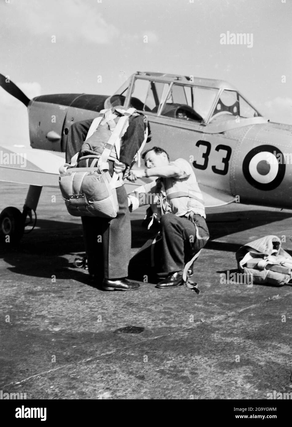 Instructor adjusting a trainee pilot's flying gear, with a de Havilland ...