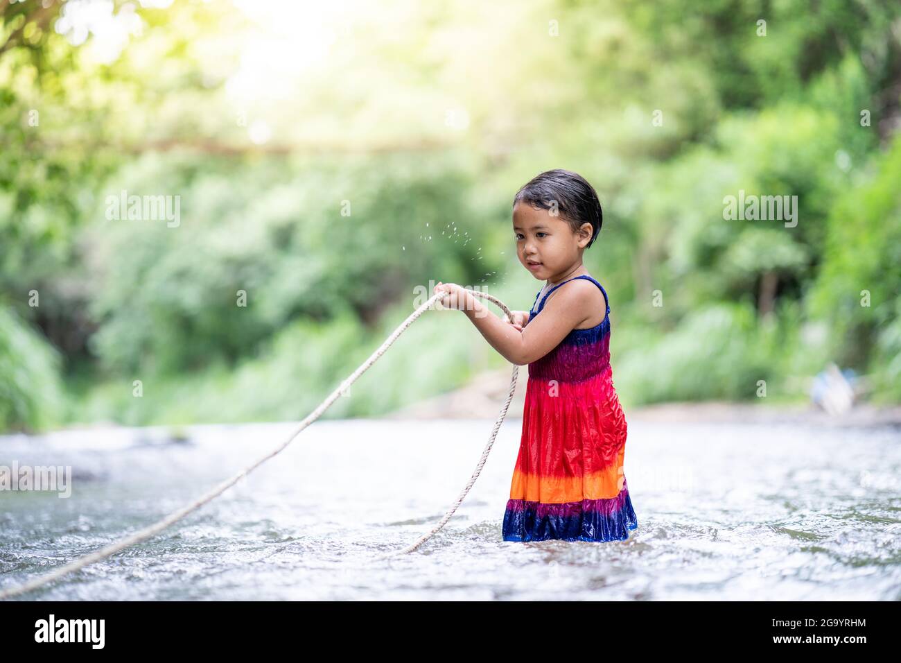 Little girl stands in the water holding a rope Stock Photo - Alamy