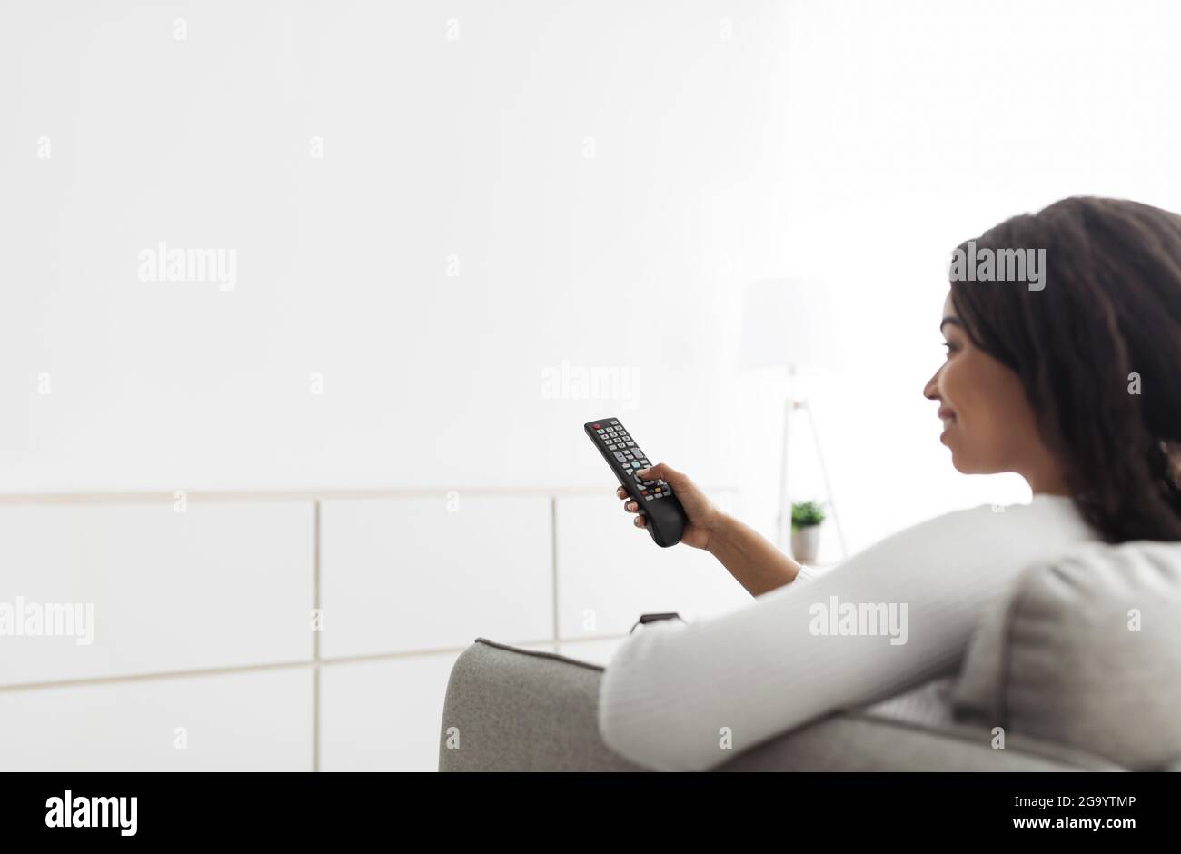Young black lady holding and pointing remote control on white empty ...