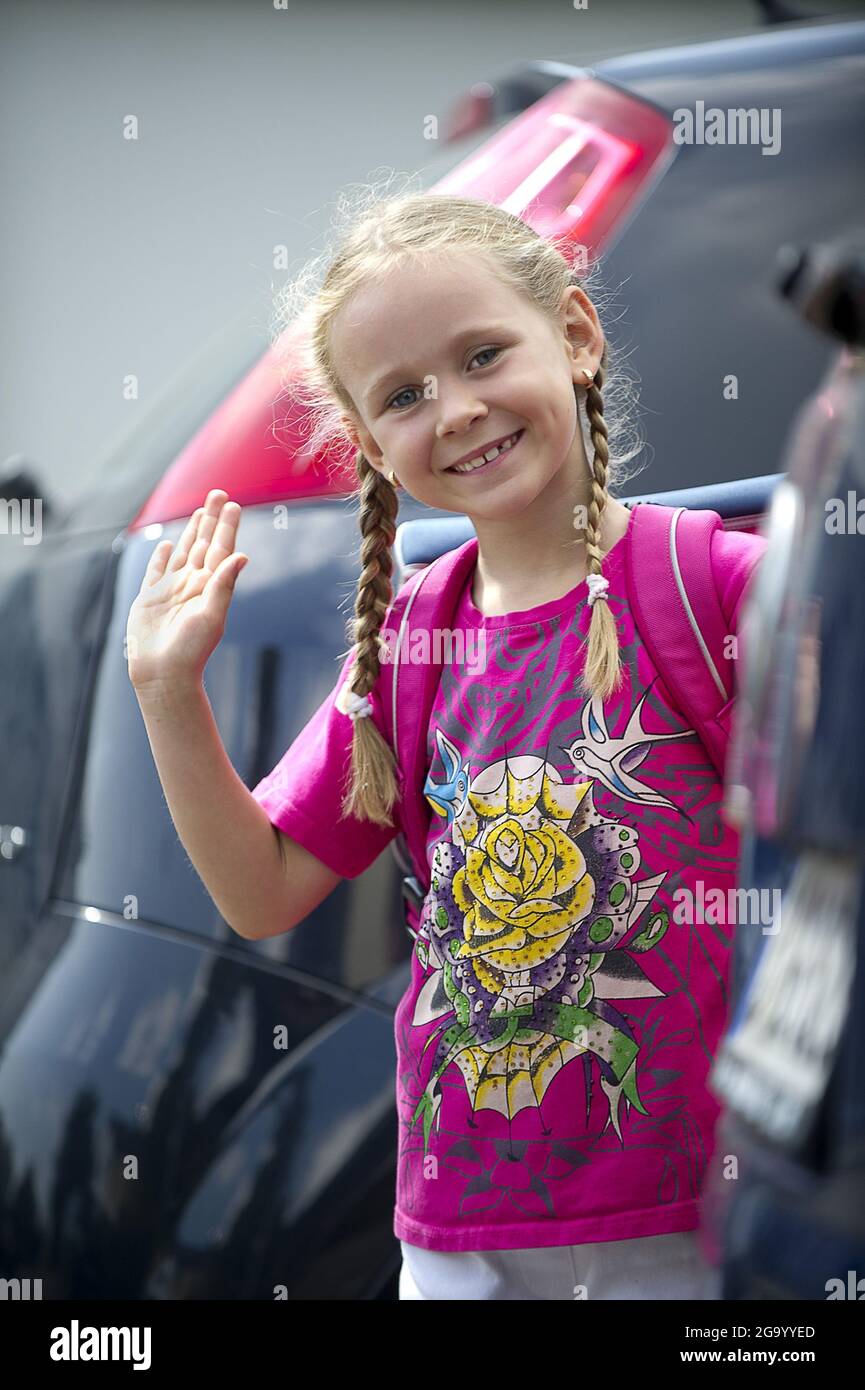 female elementary school student stands waving between cars , Germany ...