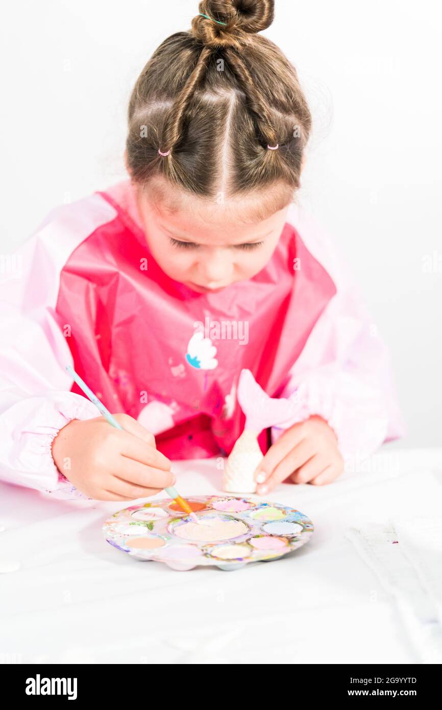 Little girl painting mermaid tails made out of modeling clay with ...