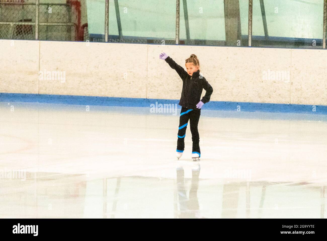 Little figure skater in black clothes practicing on the indoor ice ...