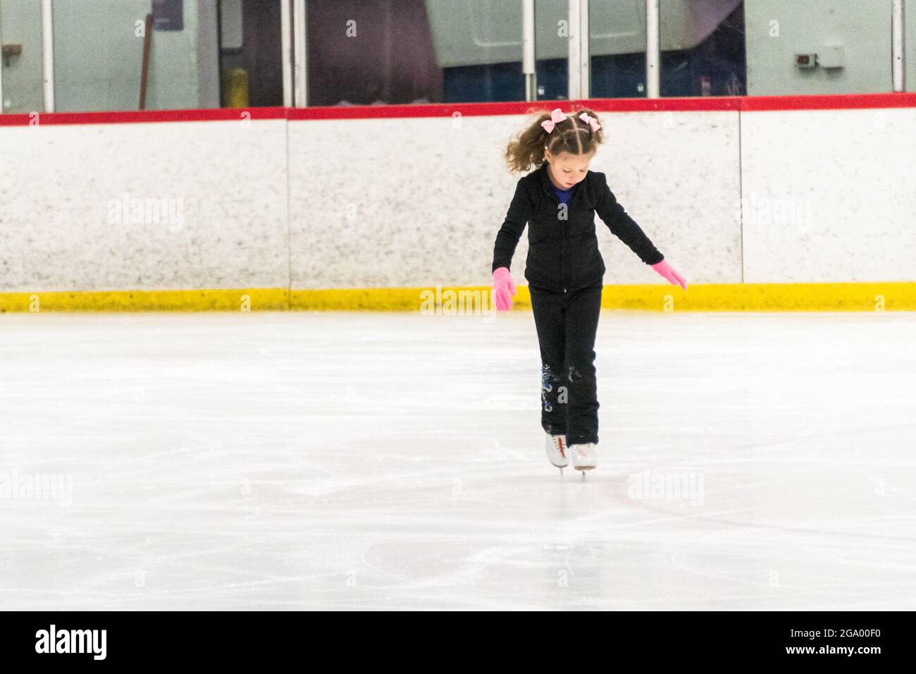 Little girl practicing figure skating moves on the indoor ice rink ...