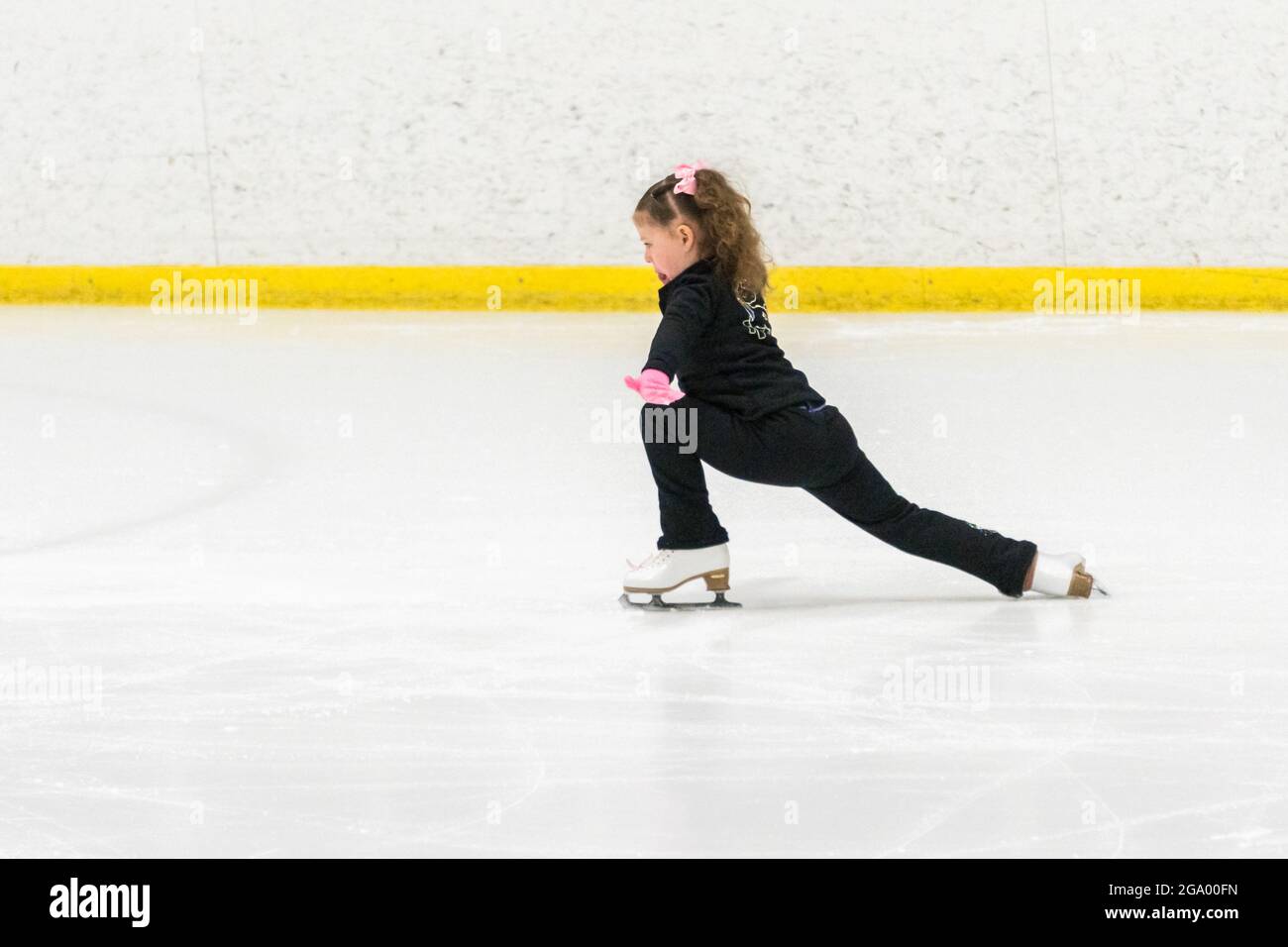 Little girl practicing figure skating moves on the indoor ice rink ...