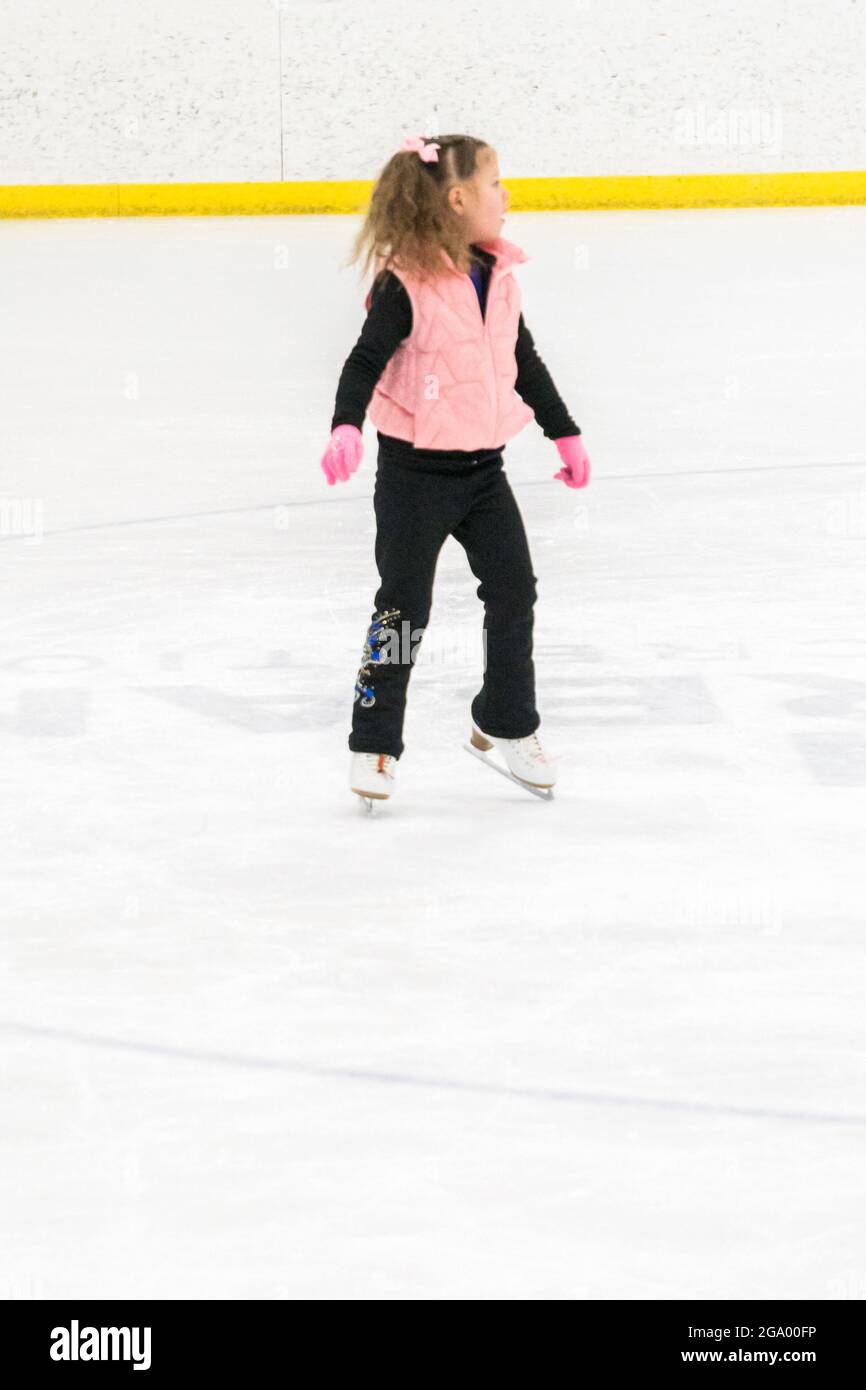Little girl practicing figure skating moves on the indoor ice rink ...