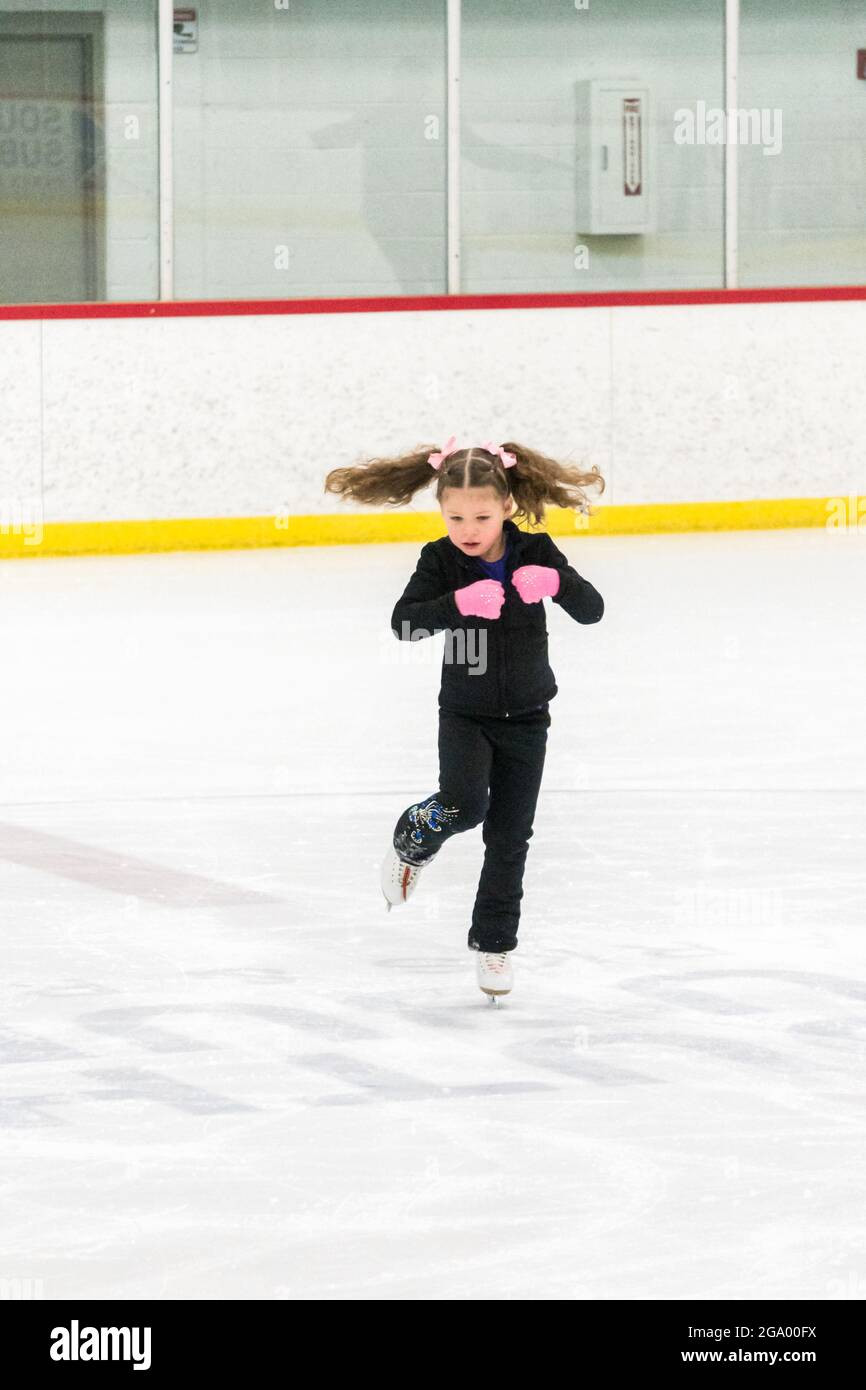 Little girl practicing figure skating moves on the indoor ice rink ...