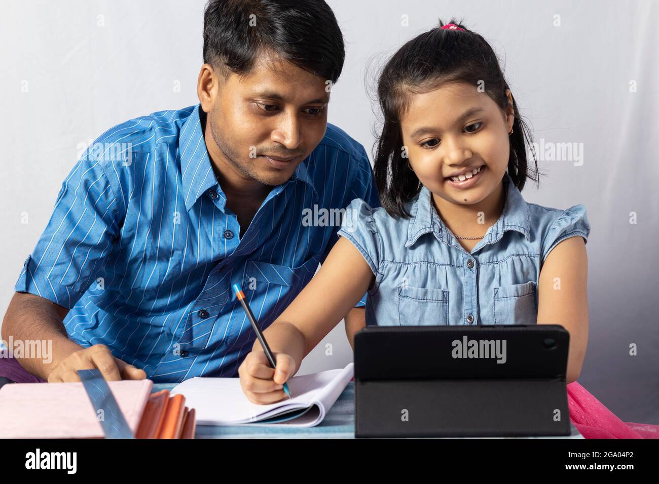 An Indian girl student studying with tablet besides her father, teacher ...