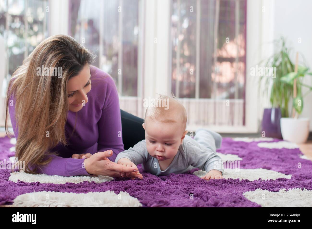 Happy mother laying down on the floor and playing with her baby boy ...