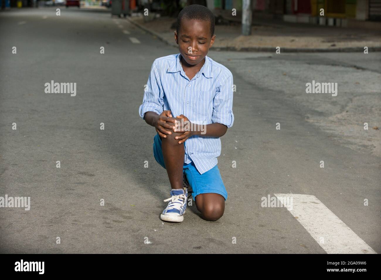 little boy fallen alone on the road crying while holding his injured ...