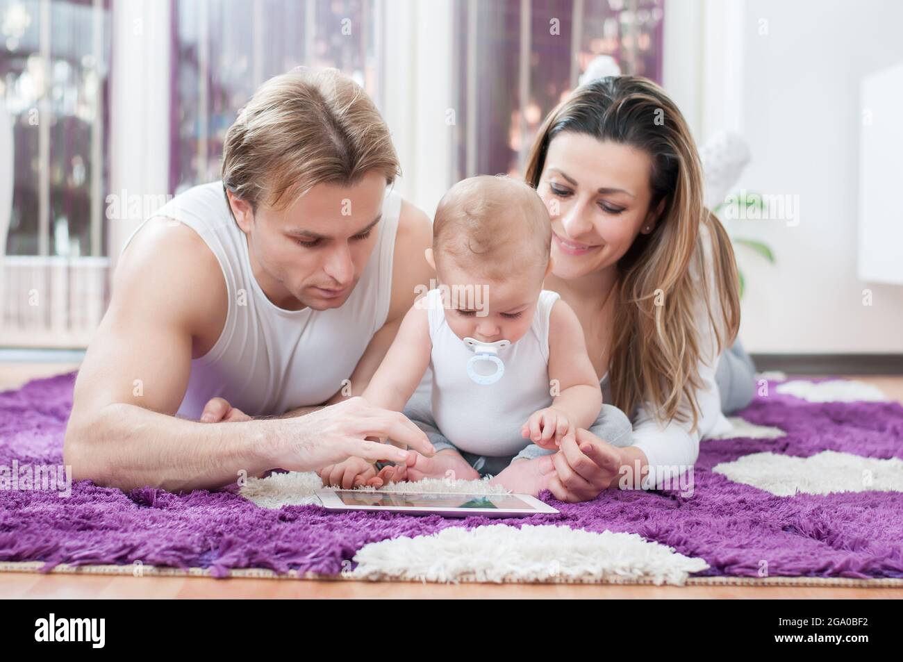 Happy parents laying down on the floor and playing with their baby boy ...