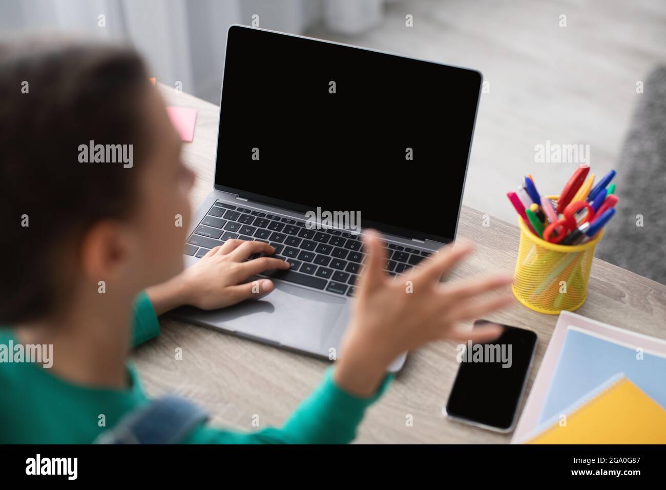 Girl sitting at desk, using blank laptop, waving hand Stock Photo - Alamy