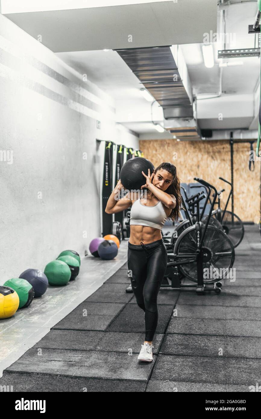 woman walking with ball shot weight on shoulder in gym doing crossfit ...