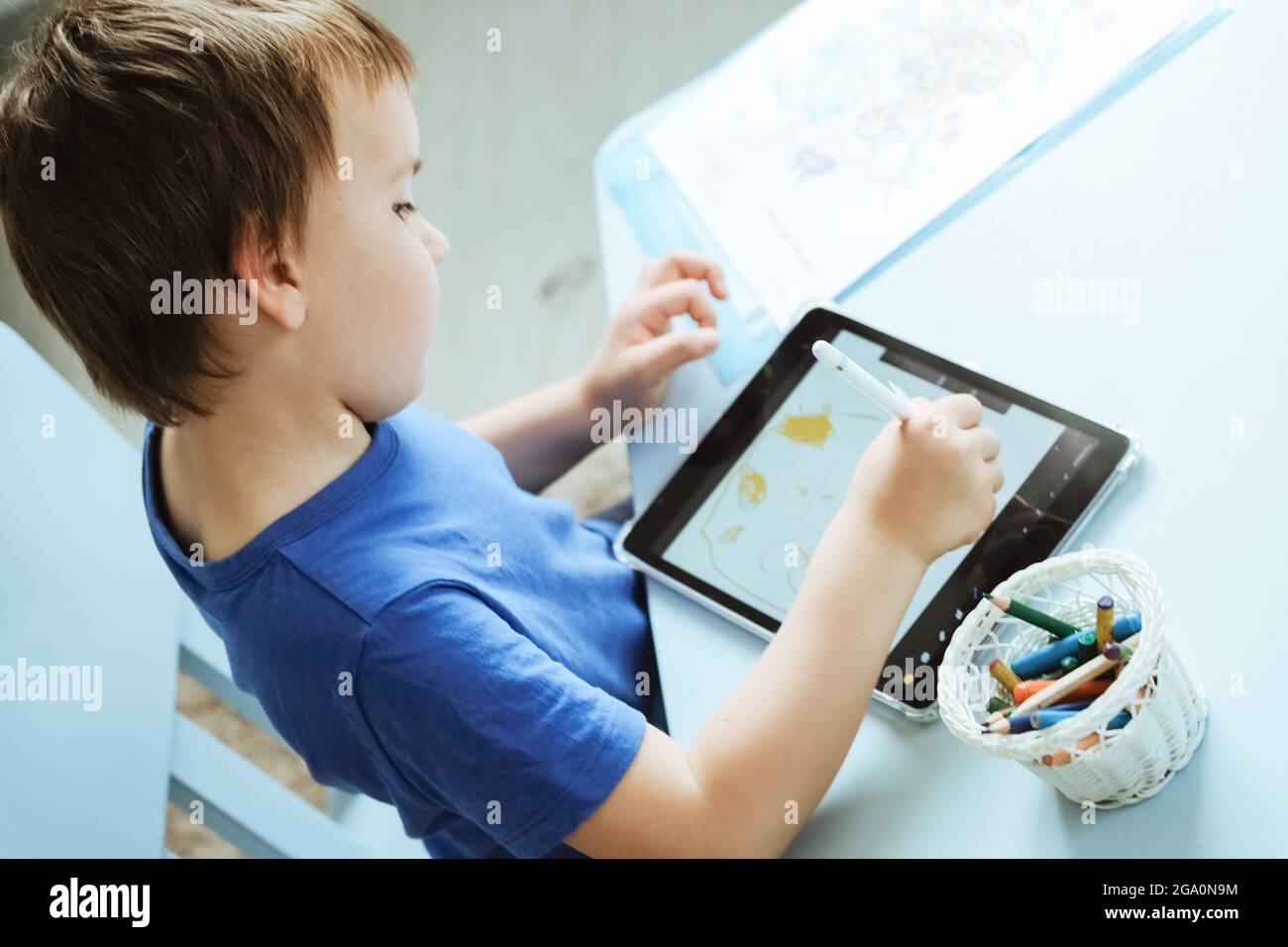 Cute boy in blue t shirt using digital tablet or computer for drawing ...
