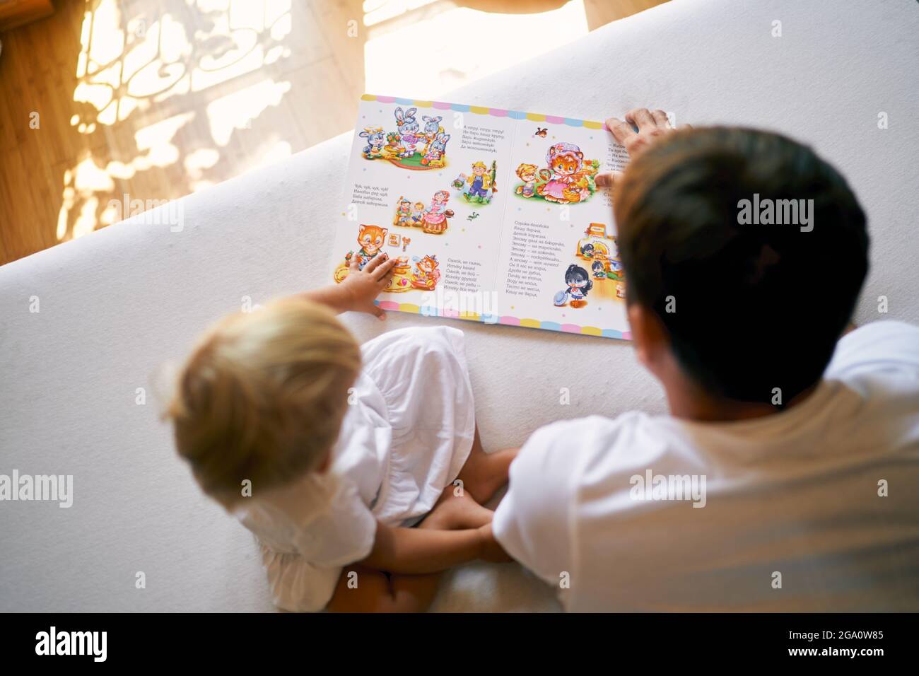 Little girl and her dad are looking at a picture book. View from above ...