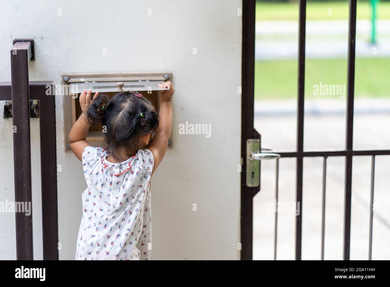 Back view of a Southeast Asian little girl opening the mailbox at the ...